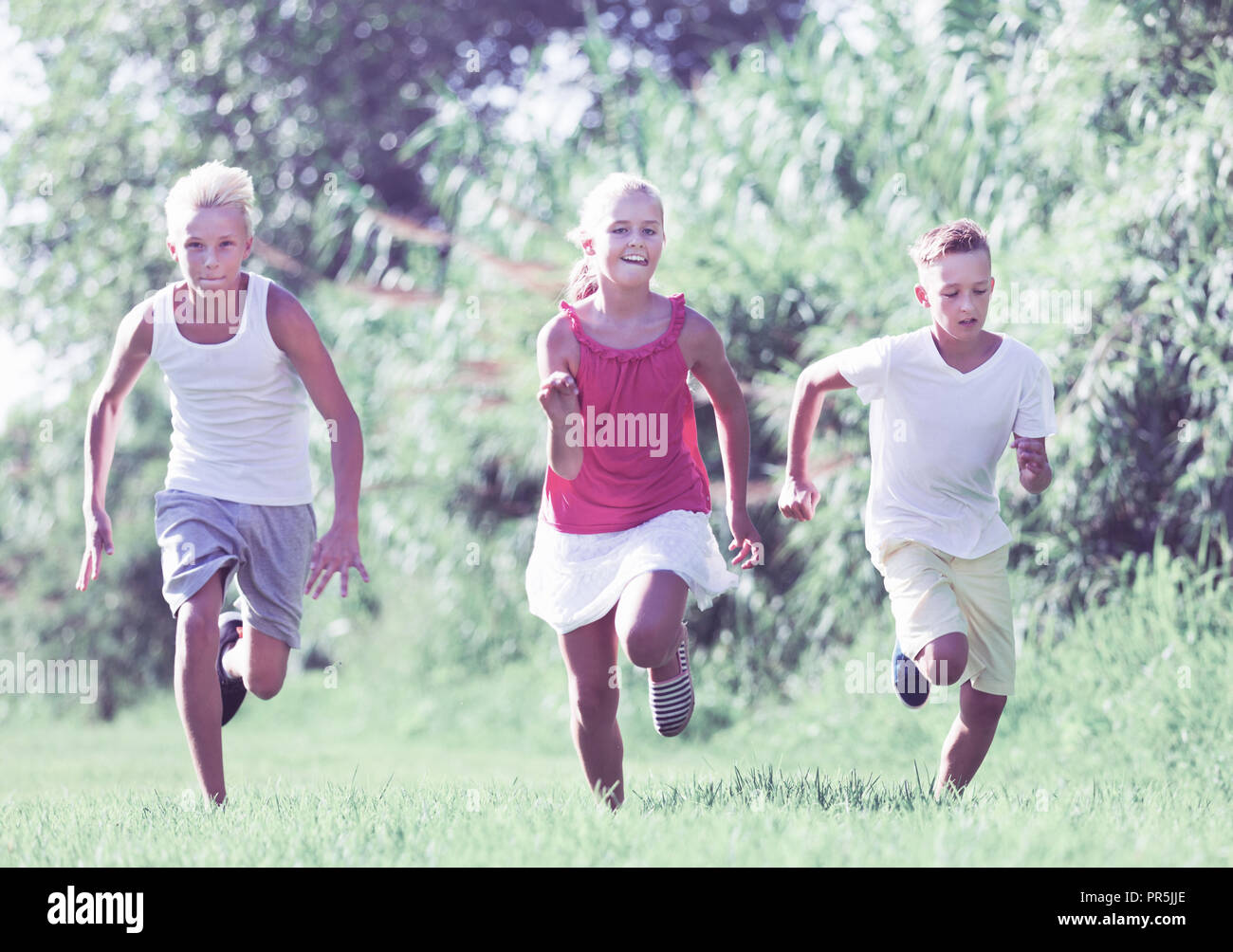 Three smiling adult kids playing active games in summer park chasing ...