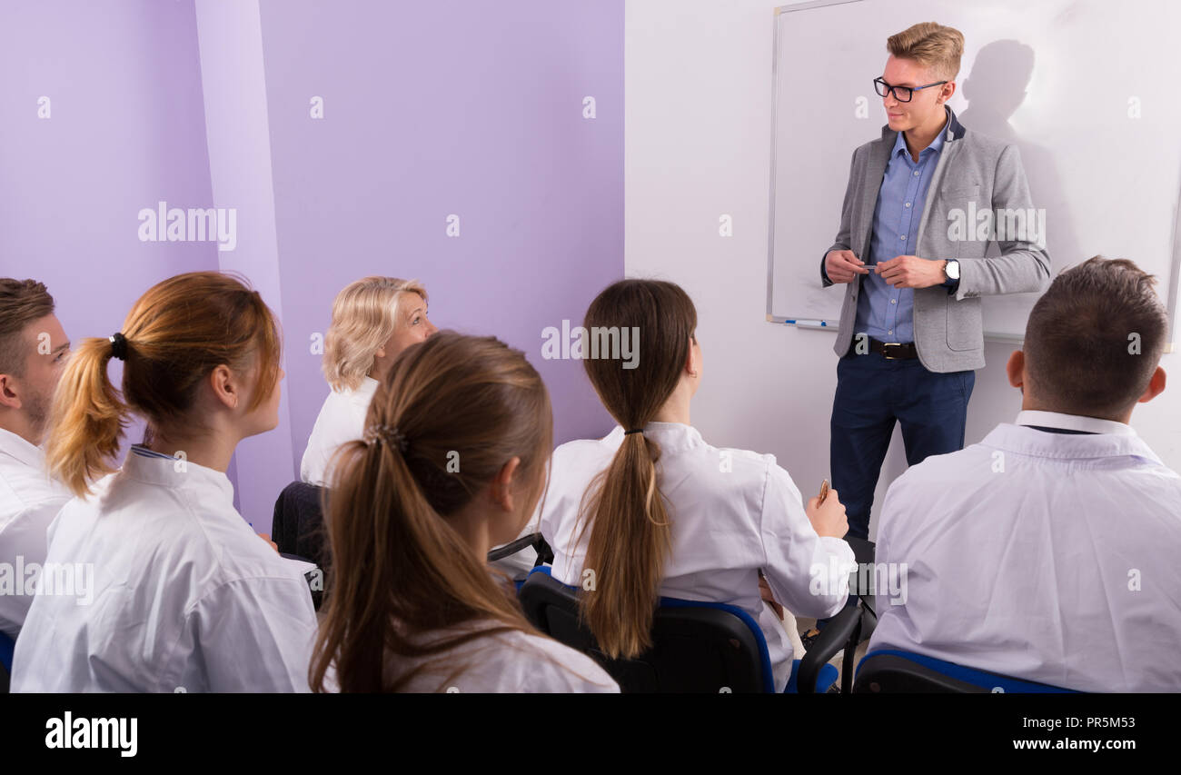 Young male student answering near whiteboard in front group of students ...