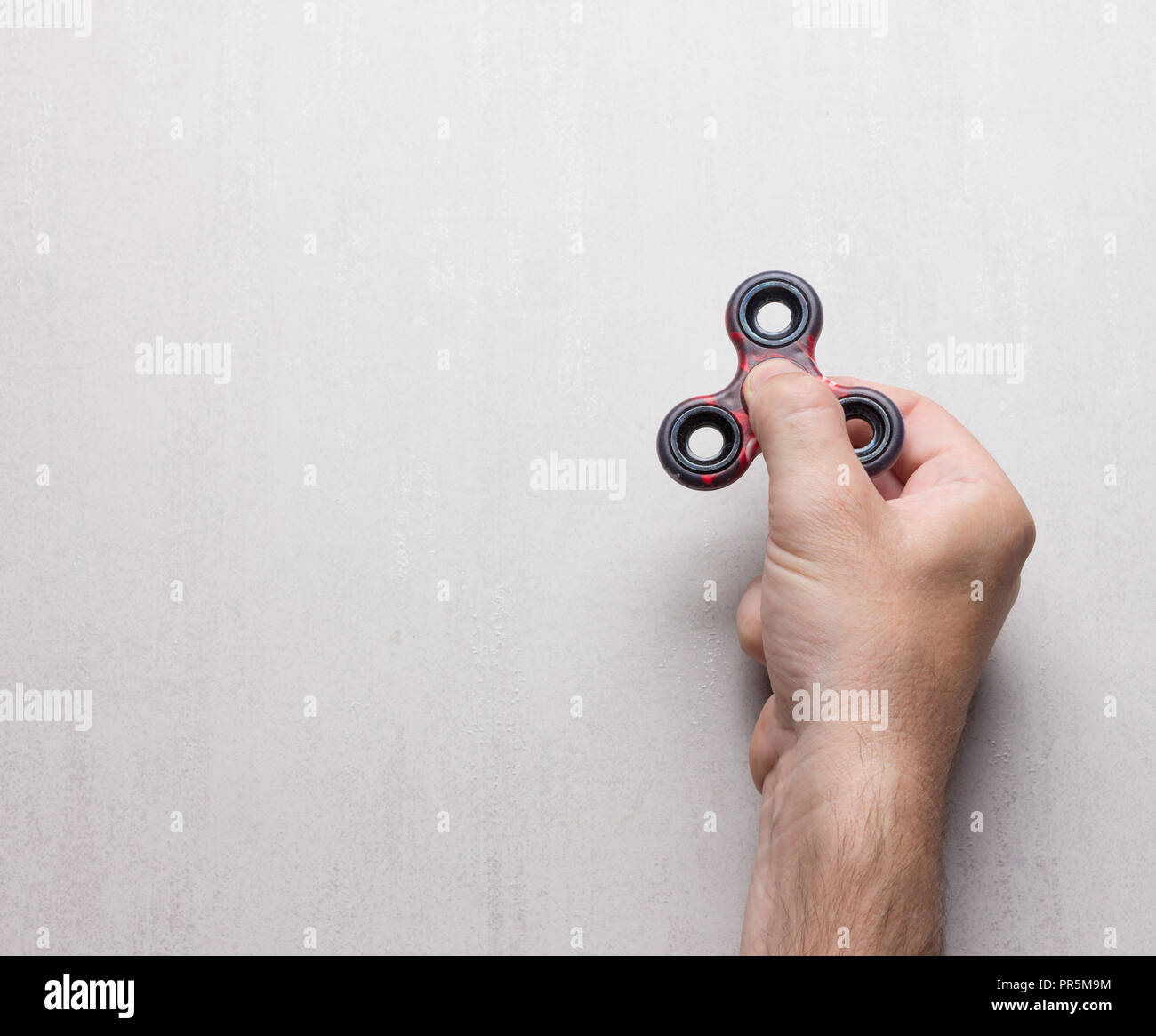 male hand with a popular toy spinner on a gray background with space ...