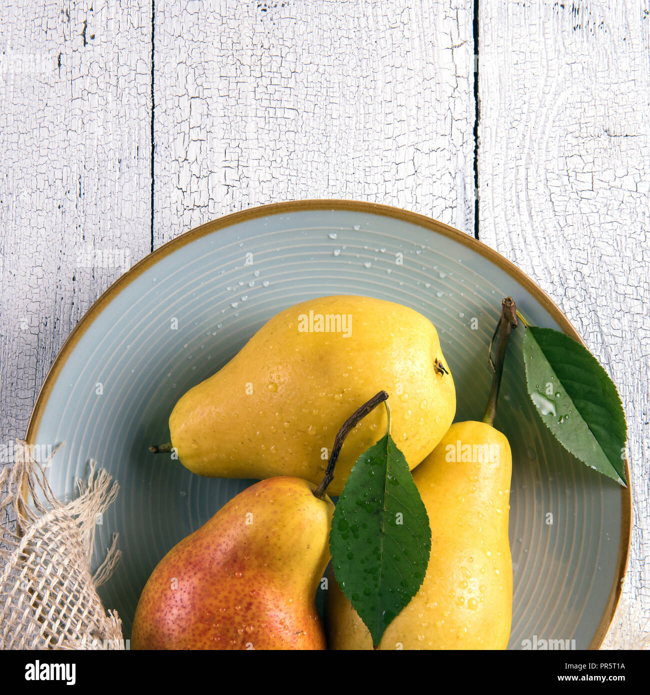 Square background with wet golden yellow pears on round blue plate on ...
