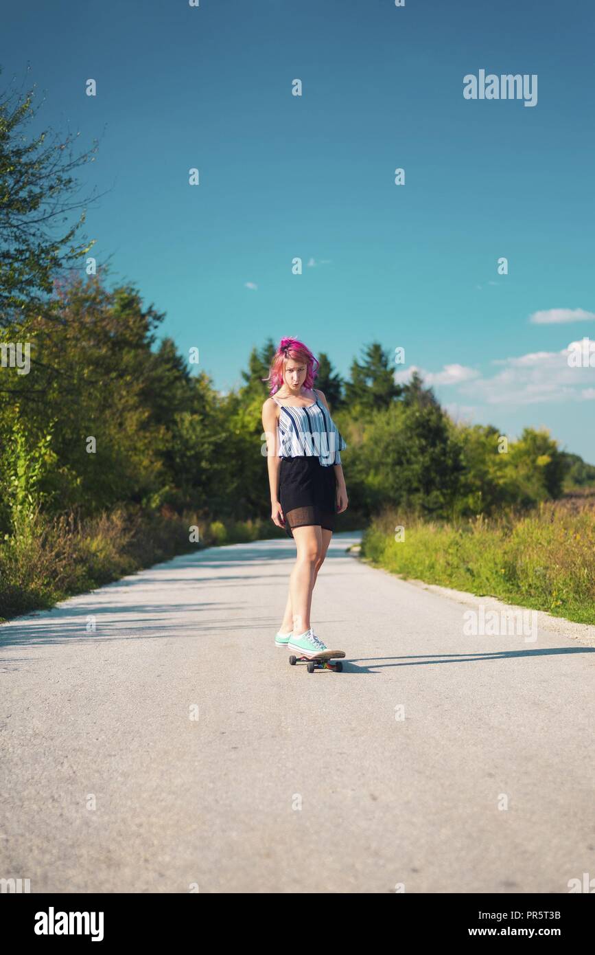 Pink haired young woman skateboarding in nature Stock Photo - Alamy