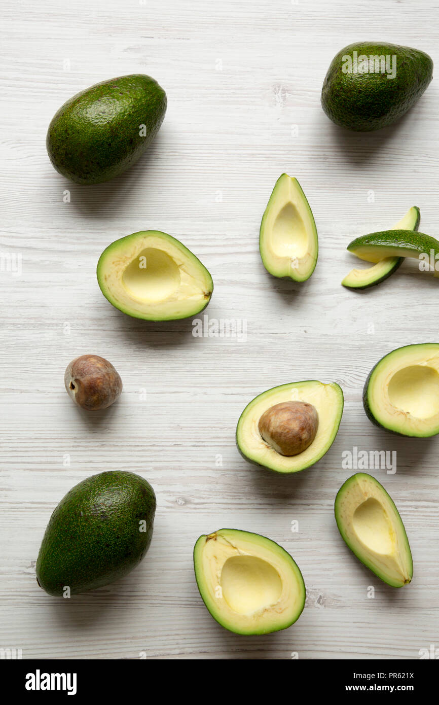 Whole and chopped avocados on white wooden background, view from above ...