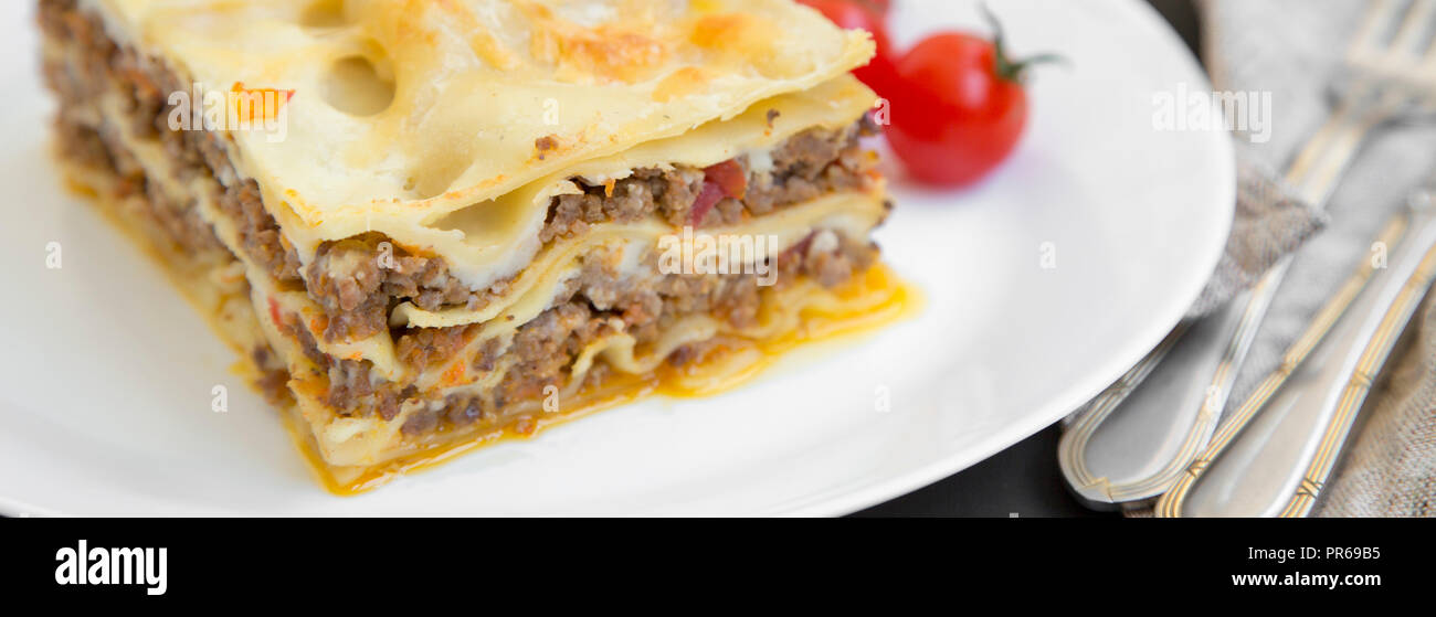 Traditional beef lasagna on a white round plate on black table, side ...