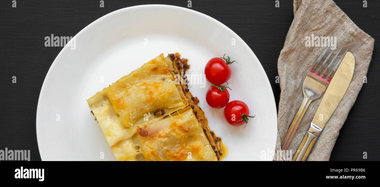 Traditional beef lasagna on a white round plate on black background ...