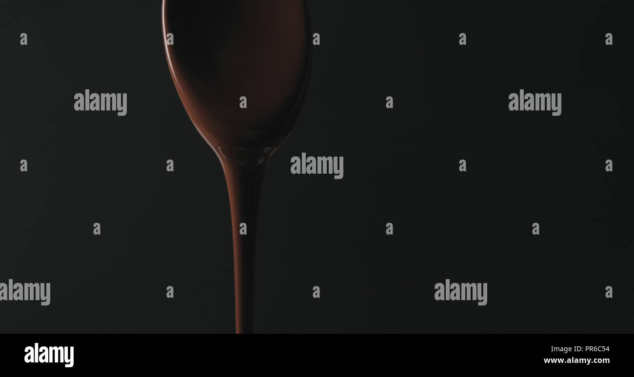 closeup melted dark chocolate dripping from spoon over black background ...