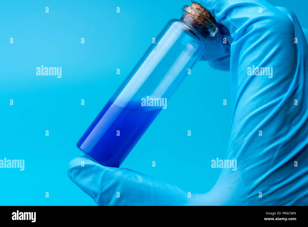 Close-up of glass tube with blue fluid in scientist hand during medical ...
