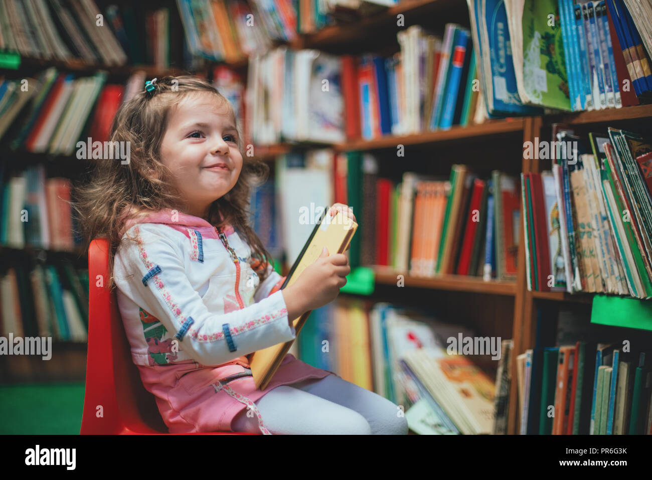 Cute girl reading book in library Stock Photo - Alamy