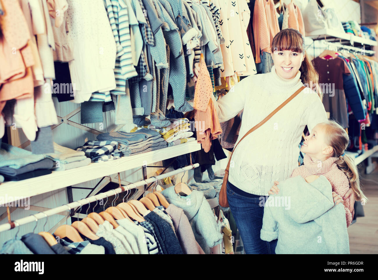 Smiling female and girl child choosing children’s clothes in store ...