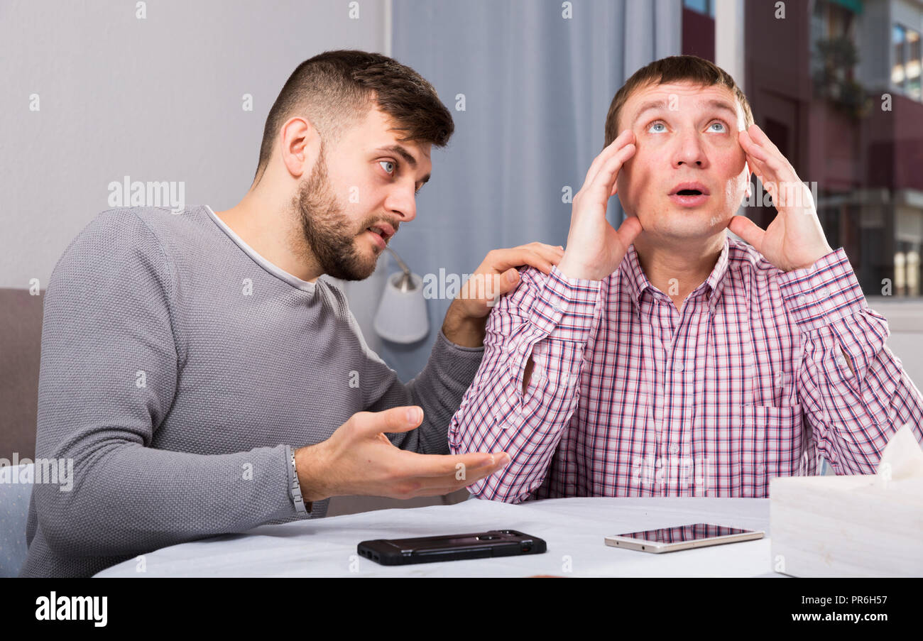 Caring friend calming distressed guy sitting at table in home interior ...
