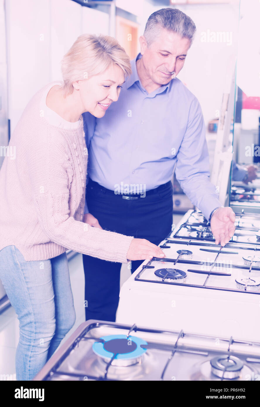 mature couple chooses in shop of household appliances gas stove with ...
