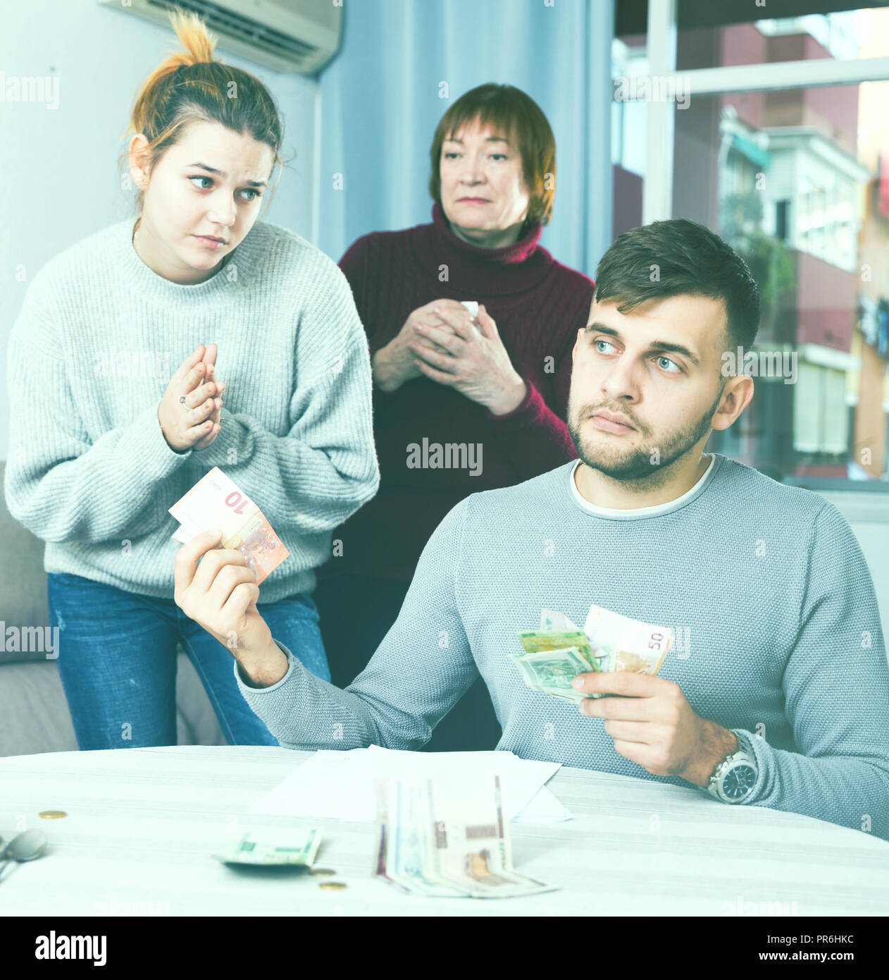 Frustrated man reluctantly giving cash to young wife standing with ...