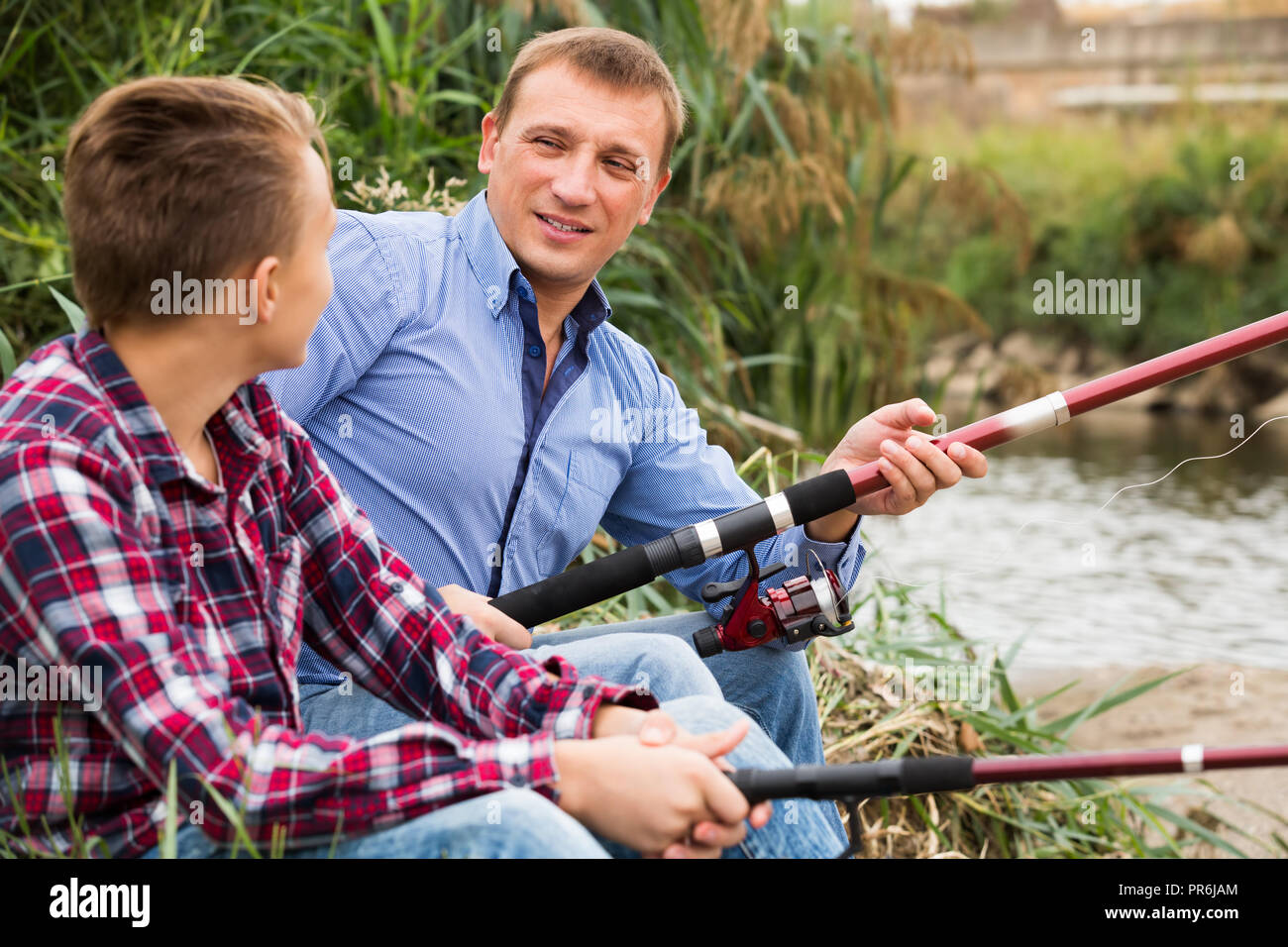 Glad father and his teenager son fishing together from water side on ...