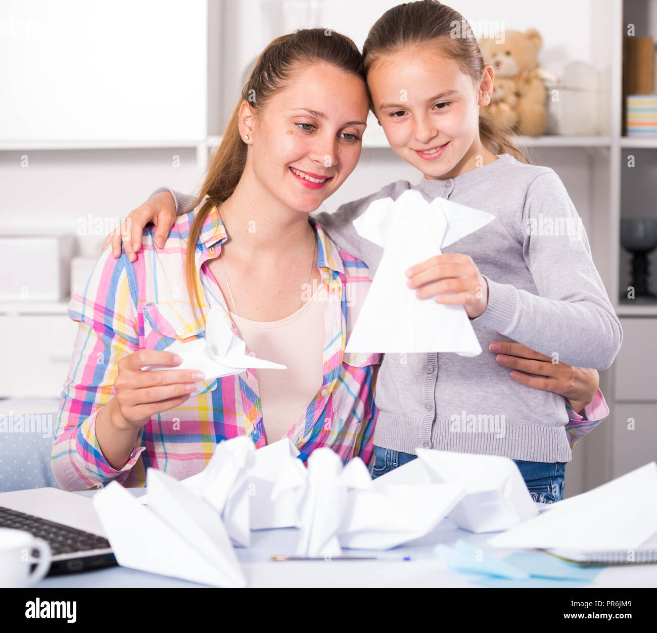 Young smiling woman and girl making airplanes of paper at home Stock ...
