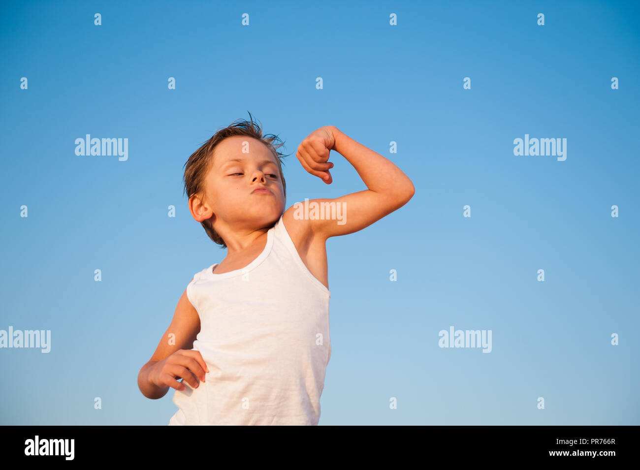 funny strong little boy showing biceps muscle with grimace on blue sky ...