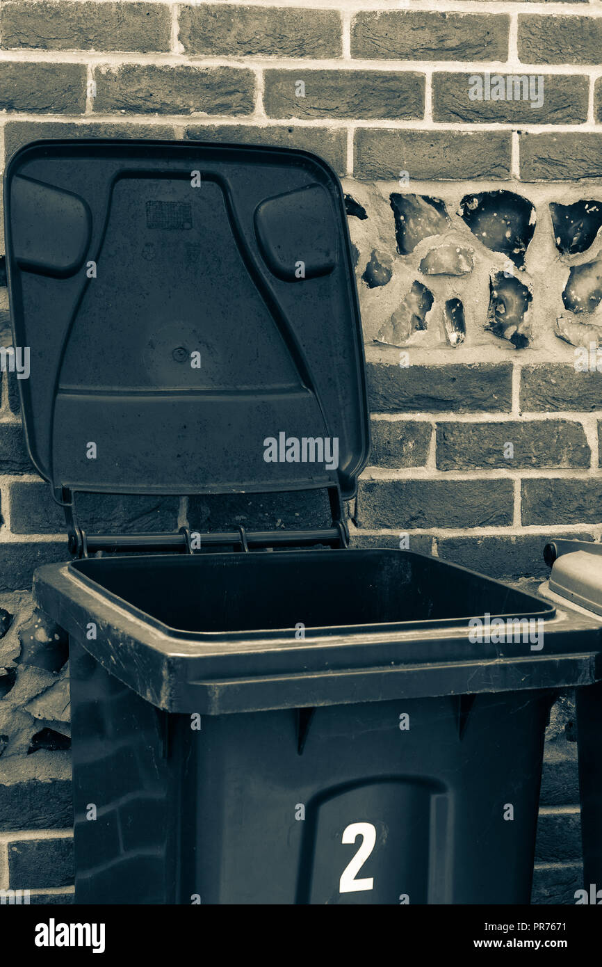 Black and white close up of a wheelie bin next to a brick and flint ...