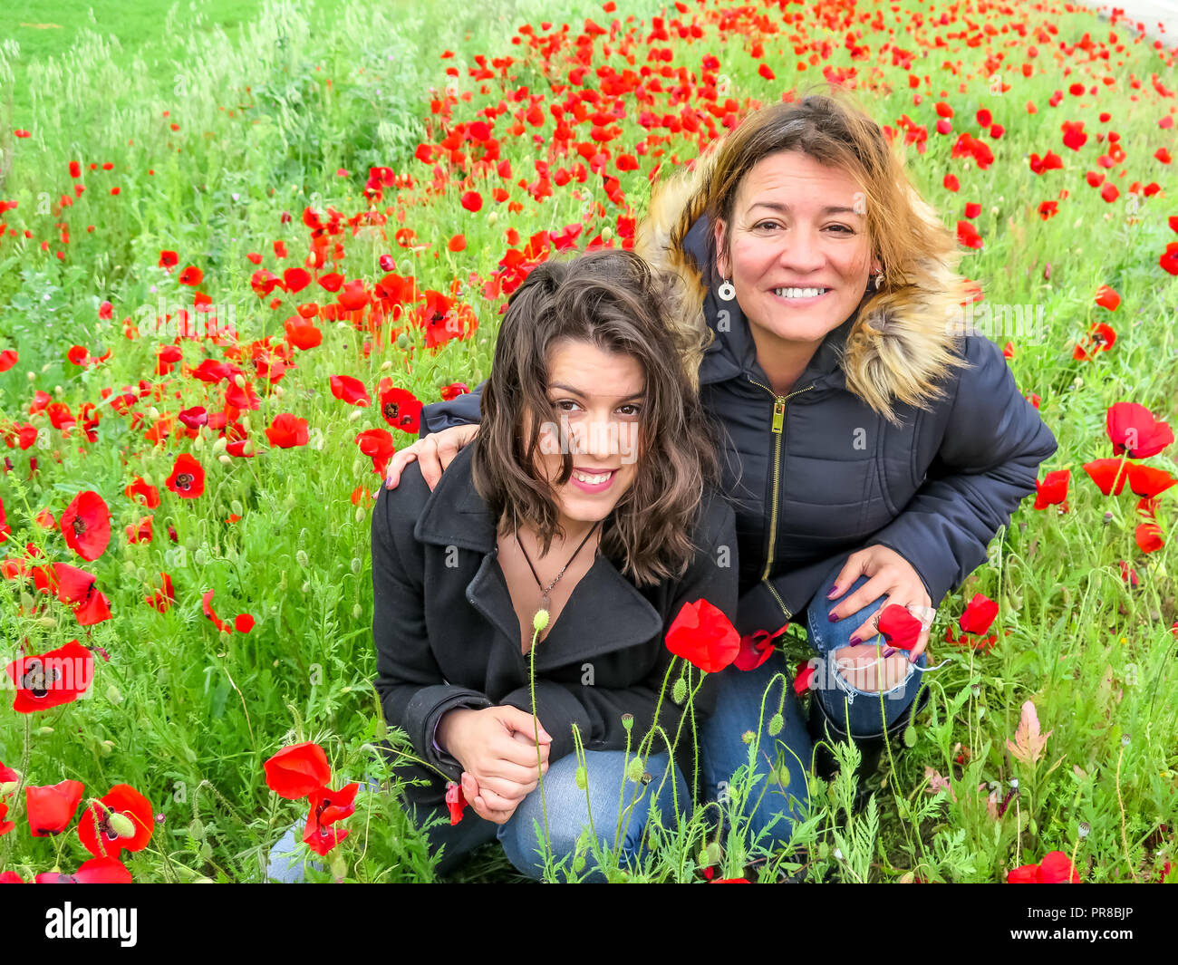 Spanish mother and young adult daugther happy & enjoying a poppy flower ...