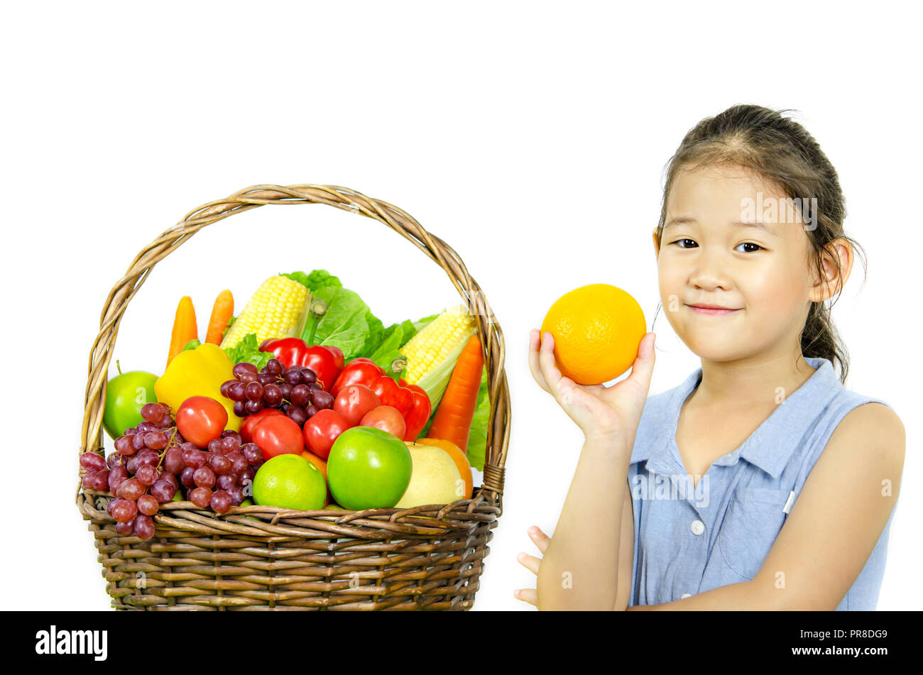 Smiling asian little girl with fruits and vegetables in basket over ...