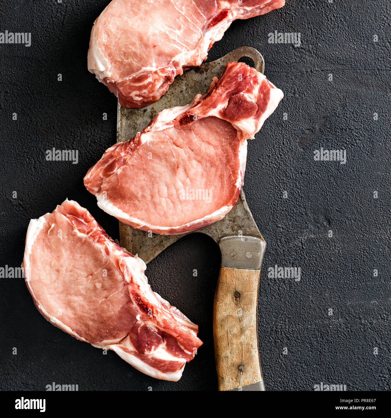 Set raw pork meat on dark stone background with butcher knife, top view ...
