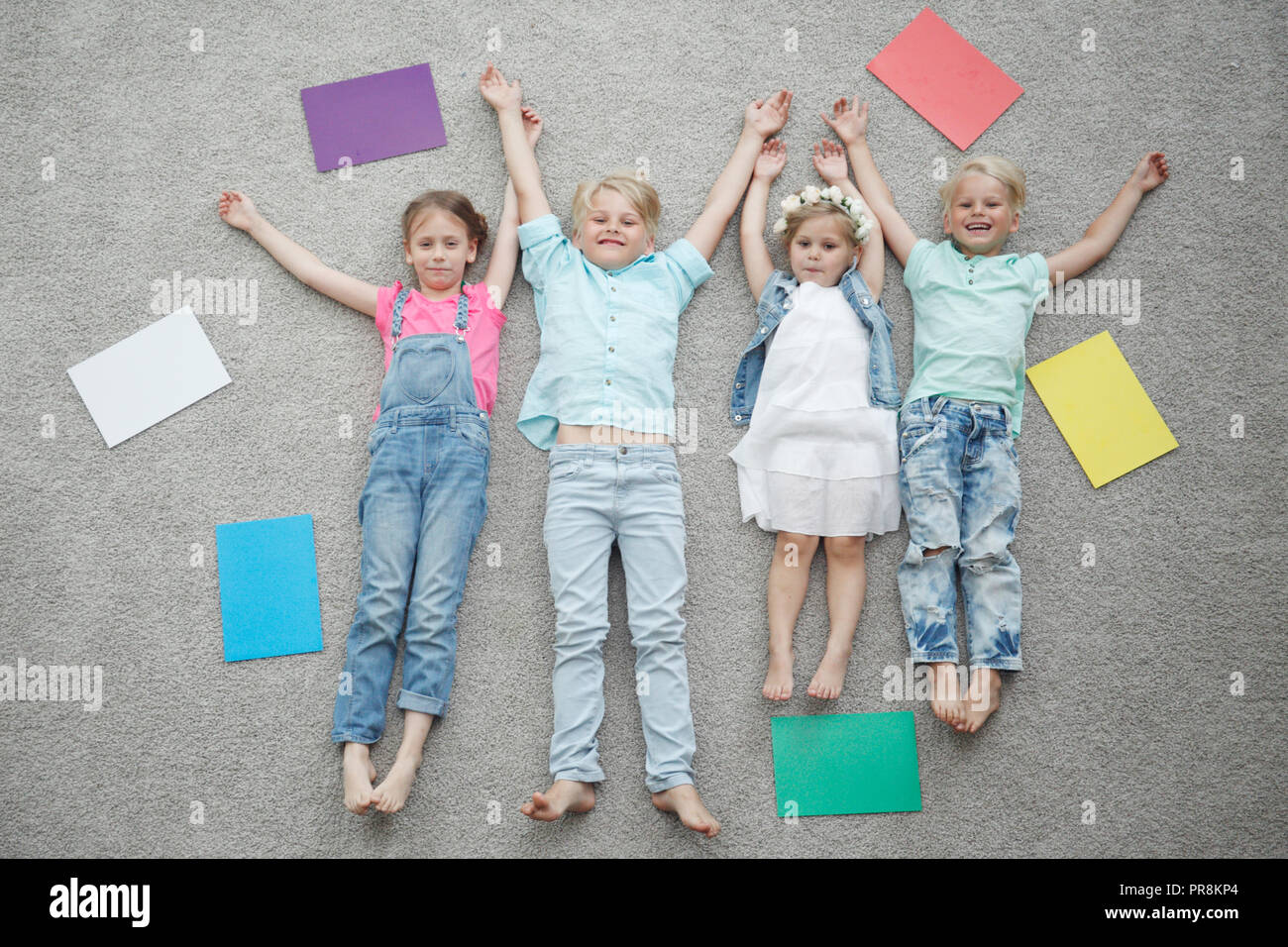 Four happy children laying on floor and smiling among colorful paper ...