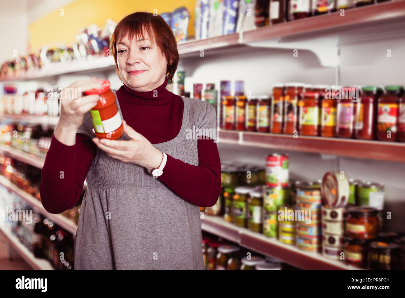 Adult female consumer holding glass jar of tomato paste in the food ...