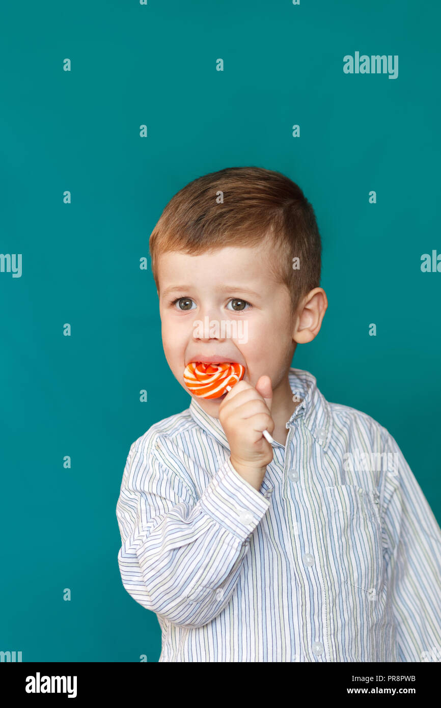 Cute child eating a lollipop on green background. Child boy eating ...