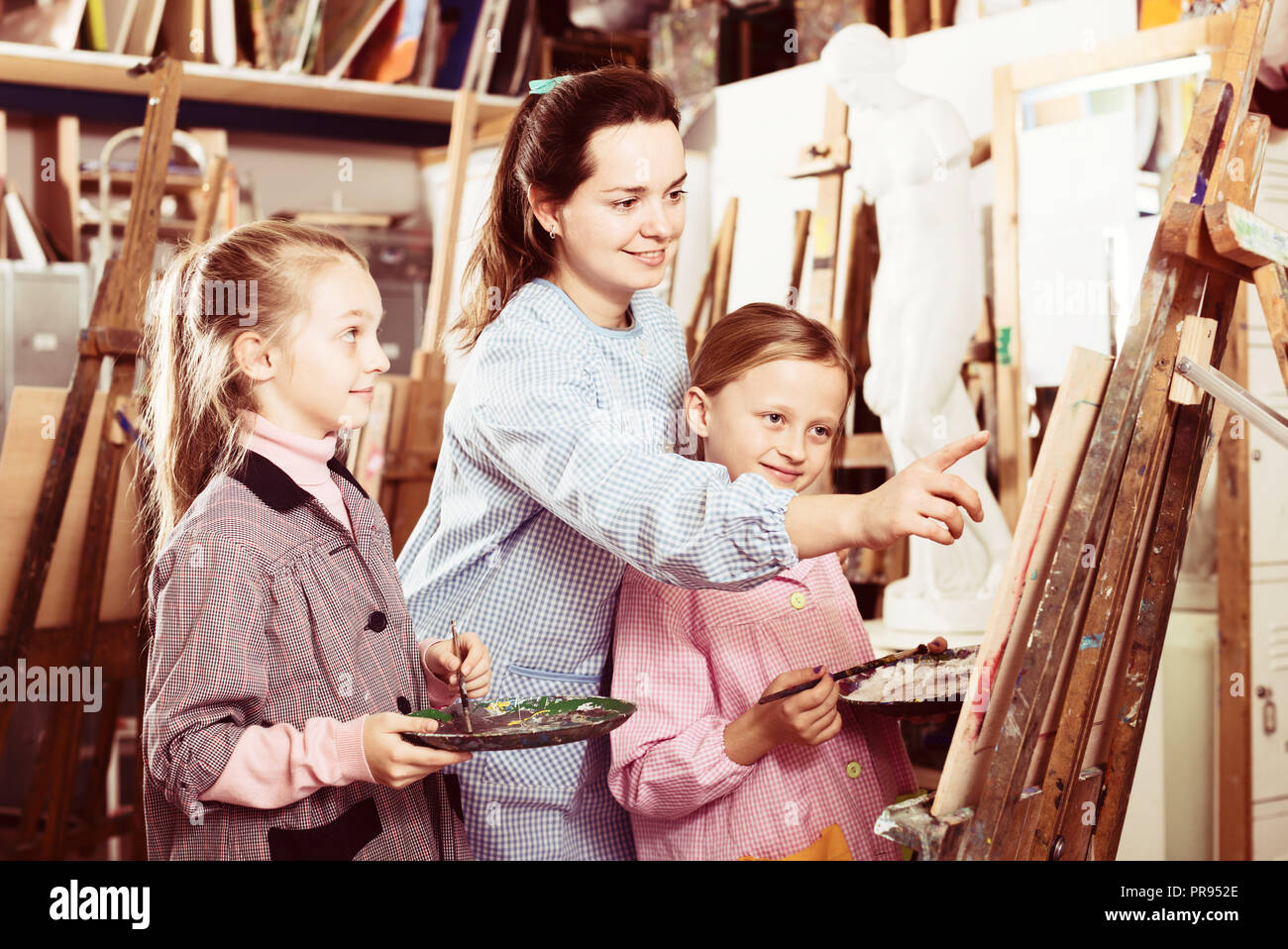 Happy female teachers assisting students during painting class at art ...