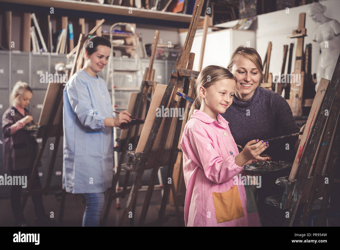Glad female teacher helping girl during painting class at art studio ...