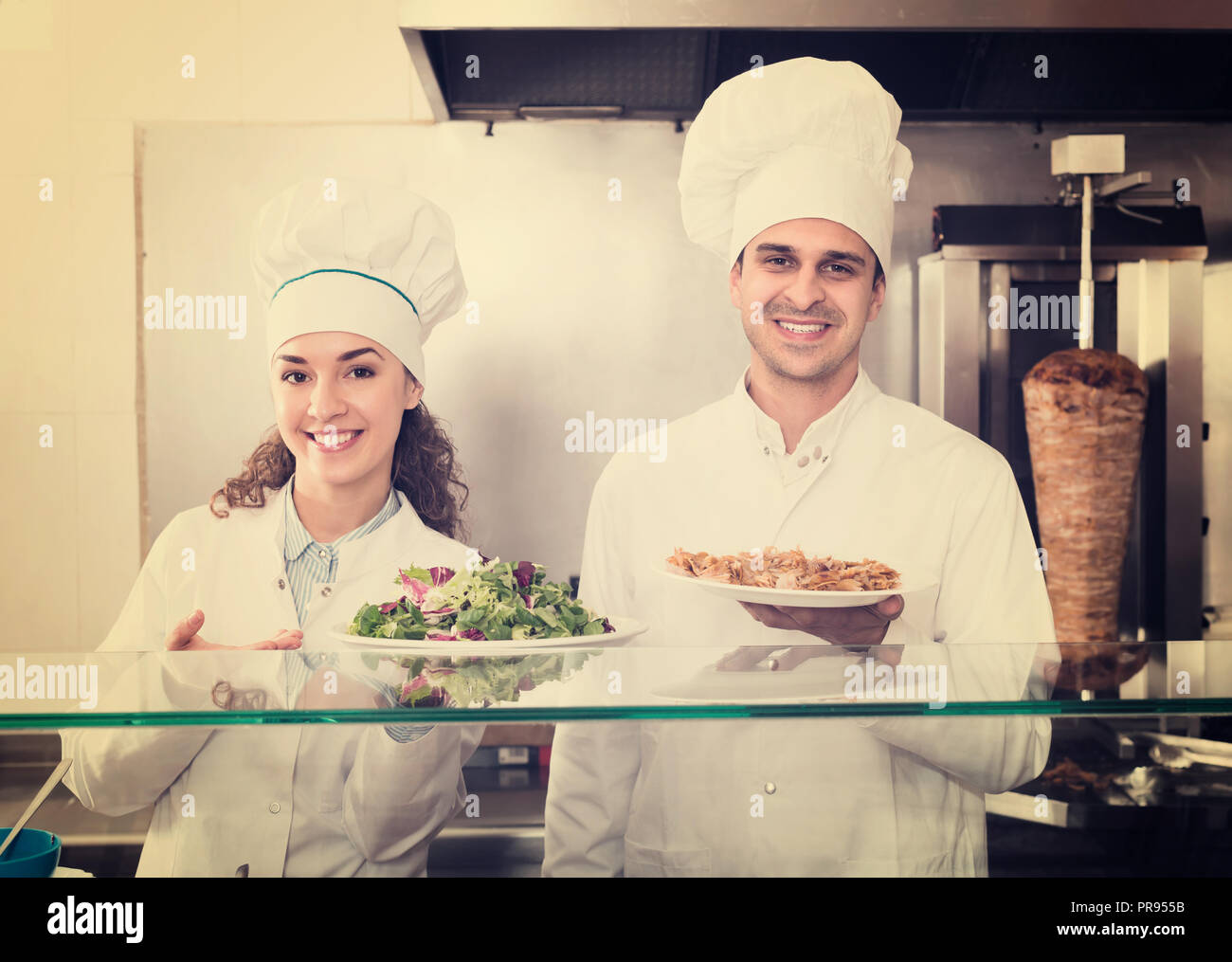 Two friendly smiling chefs offering kebab and vegetables salad at ...