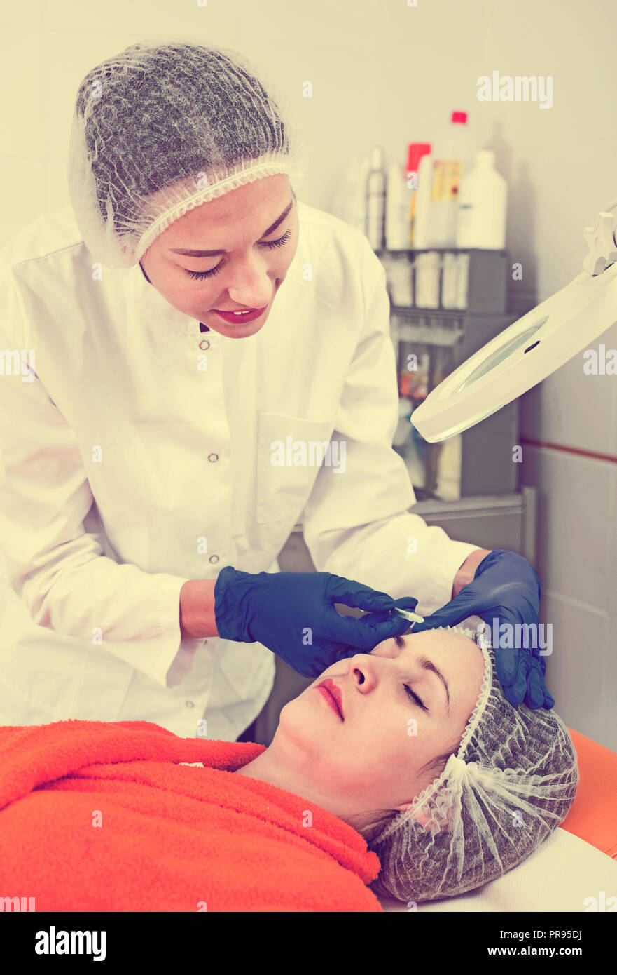 Smiling efficient female doctor doing beauty injection to young woman ...