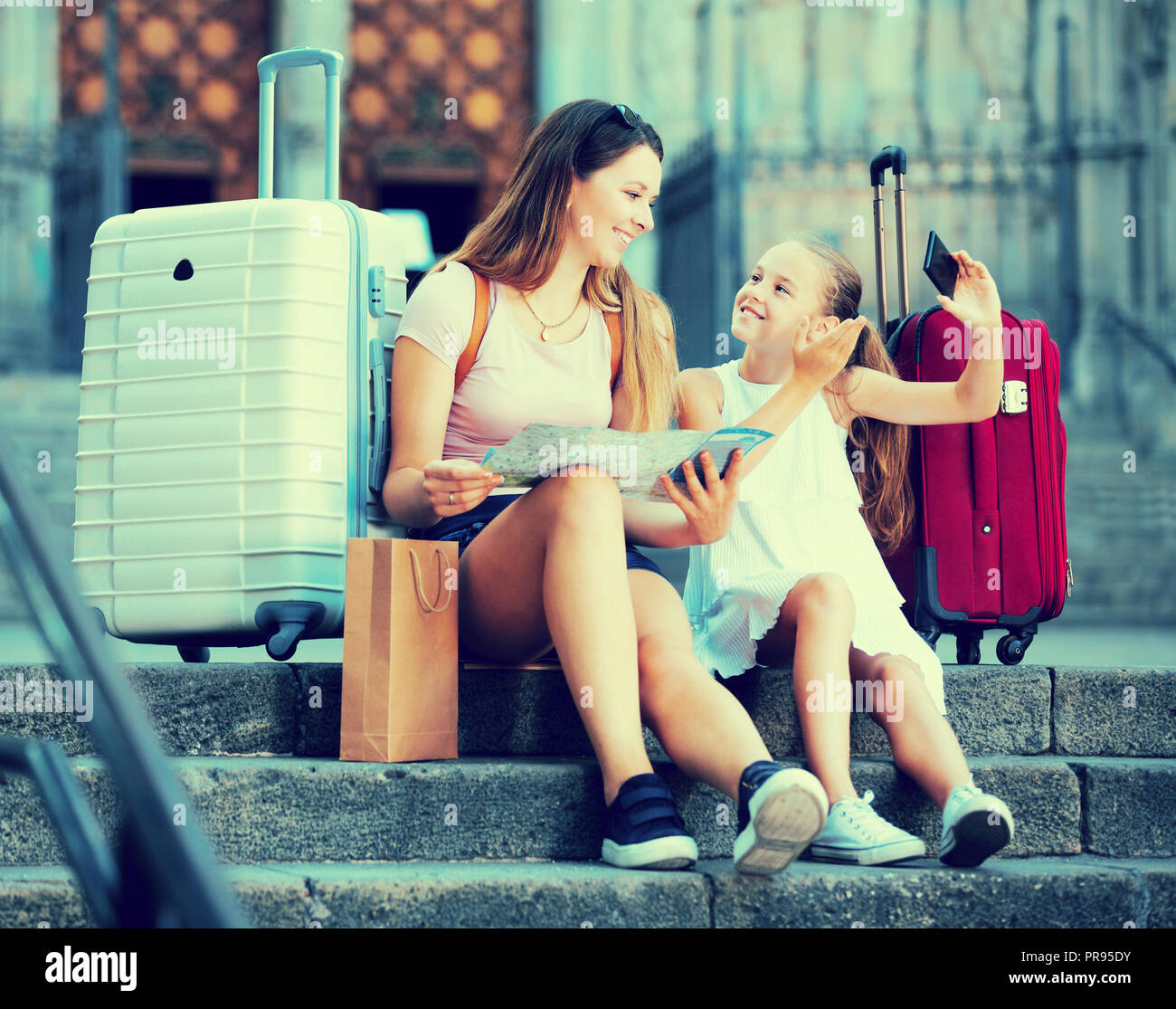 Happy mother looking map while daughter photographing sights during ...