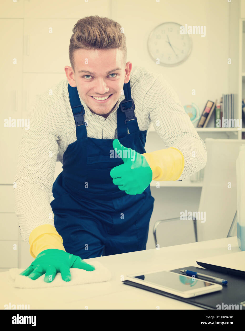 Young male janitor dusting office desk and smiling indoors Stock Photo ...