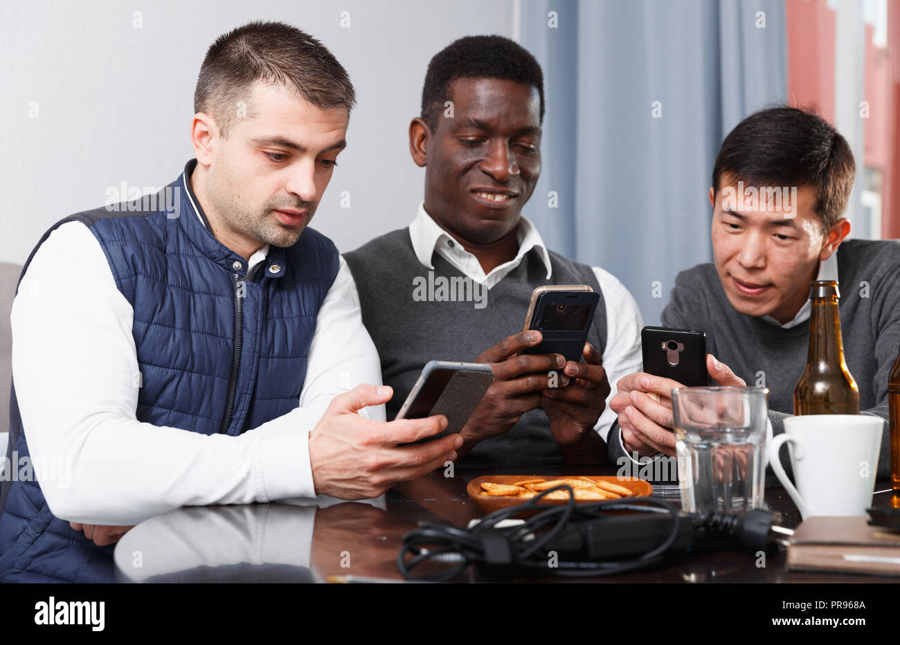 Three friends are chatting each in his phone while relaxing together at ...