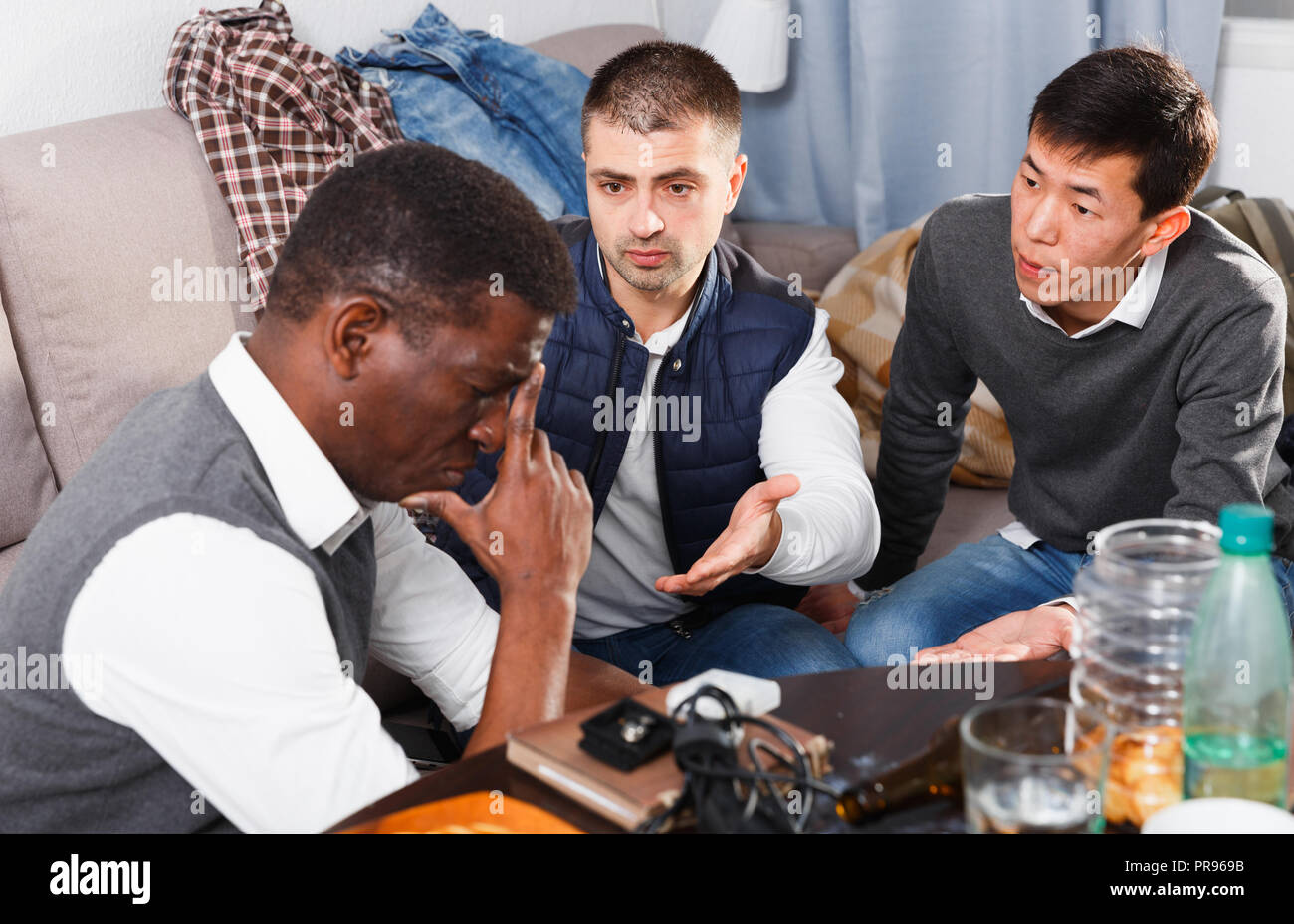 Caring friends calming distressed guy sitting together in home interior ...