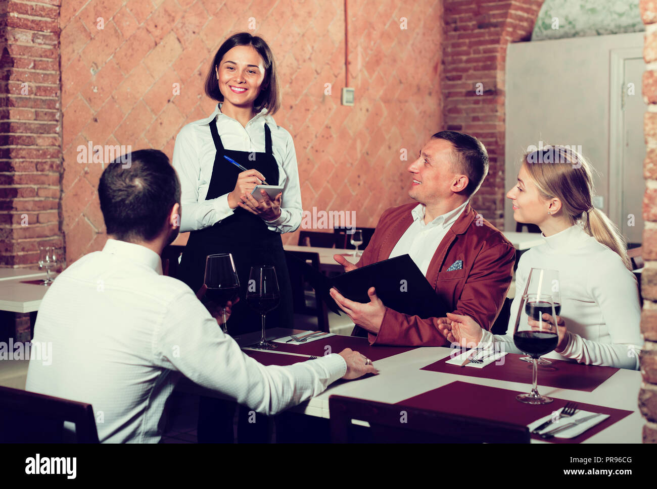 polite woman waiter receiving order from guests in country restaurant ...