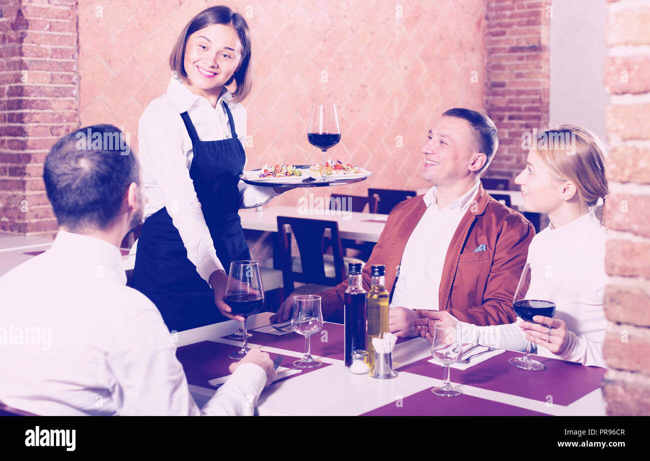 Happy female waiter carrying order for visitors in country restaurant ...