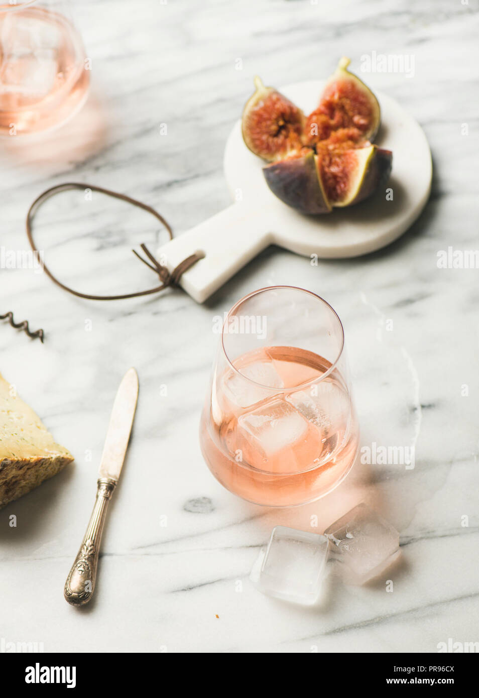 Glass of rose wine with ice cubes, cheese and fresh figs on board over ...