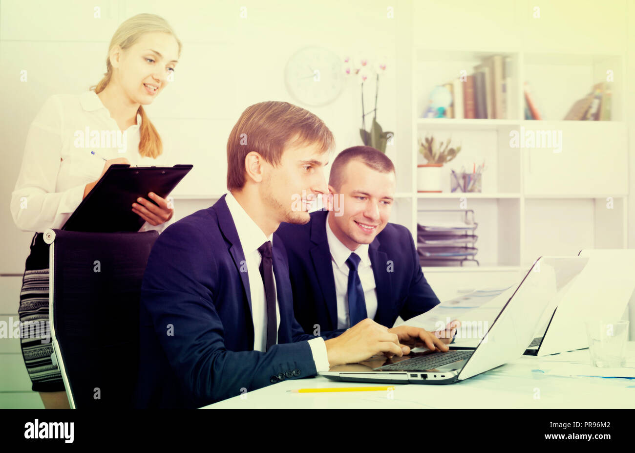 Two adult business male assistants working using laptops and woman with ...