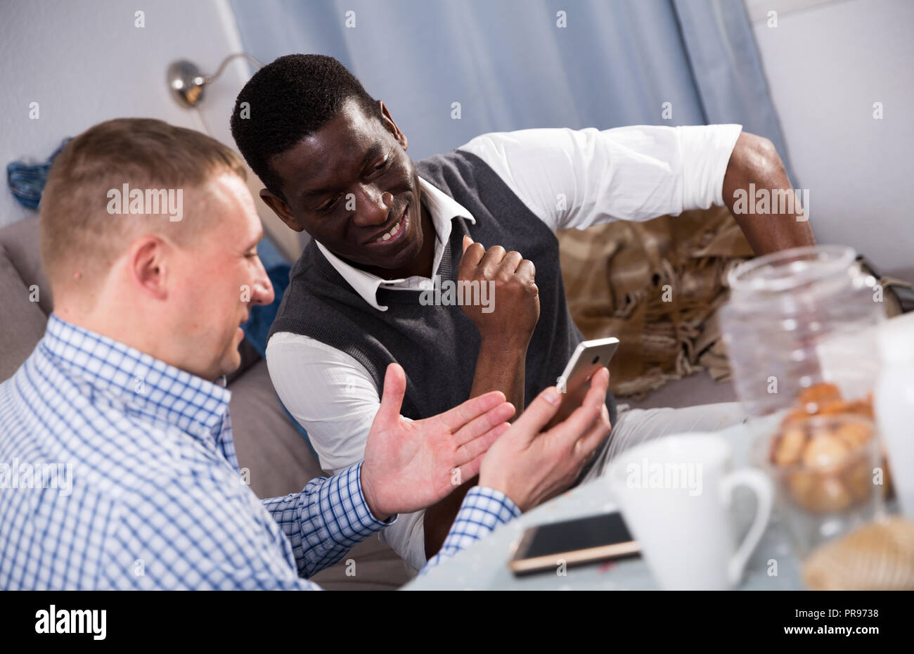Happy African man lively conversing with male at home using phone Stock ...