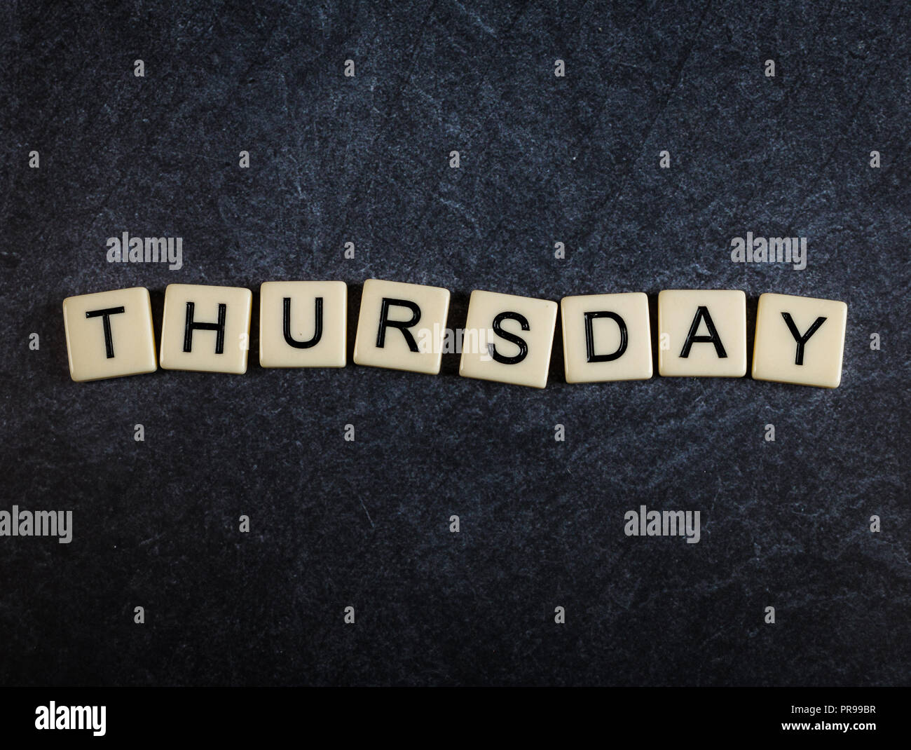 Scrabble letter tiles on black slate background spelling Thursday Stock ...
