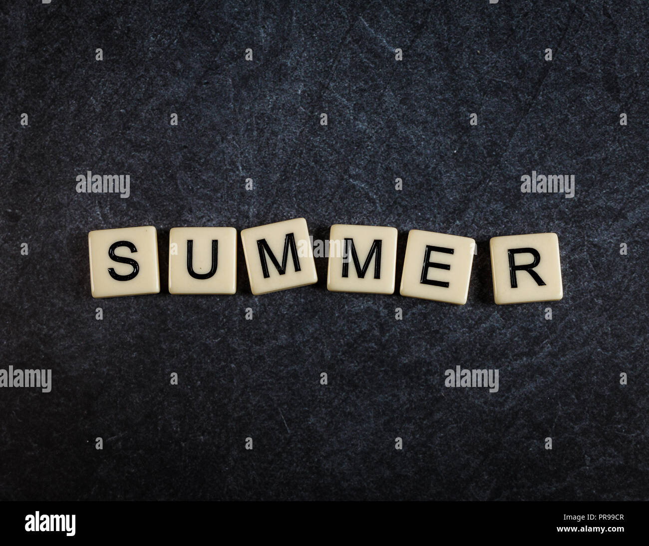 Scrabble letter tiles on black slate background spelling Summer Stock ...