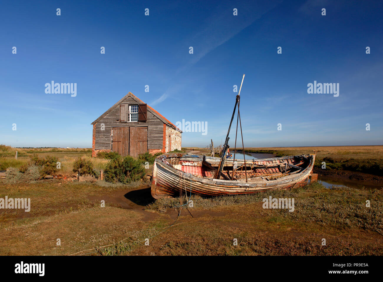 Thornham Staithe Coal Barn and harbour with derelict boat and blue sky ...