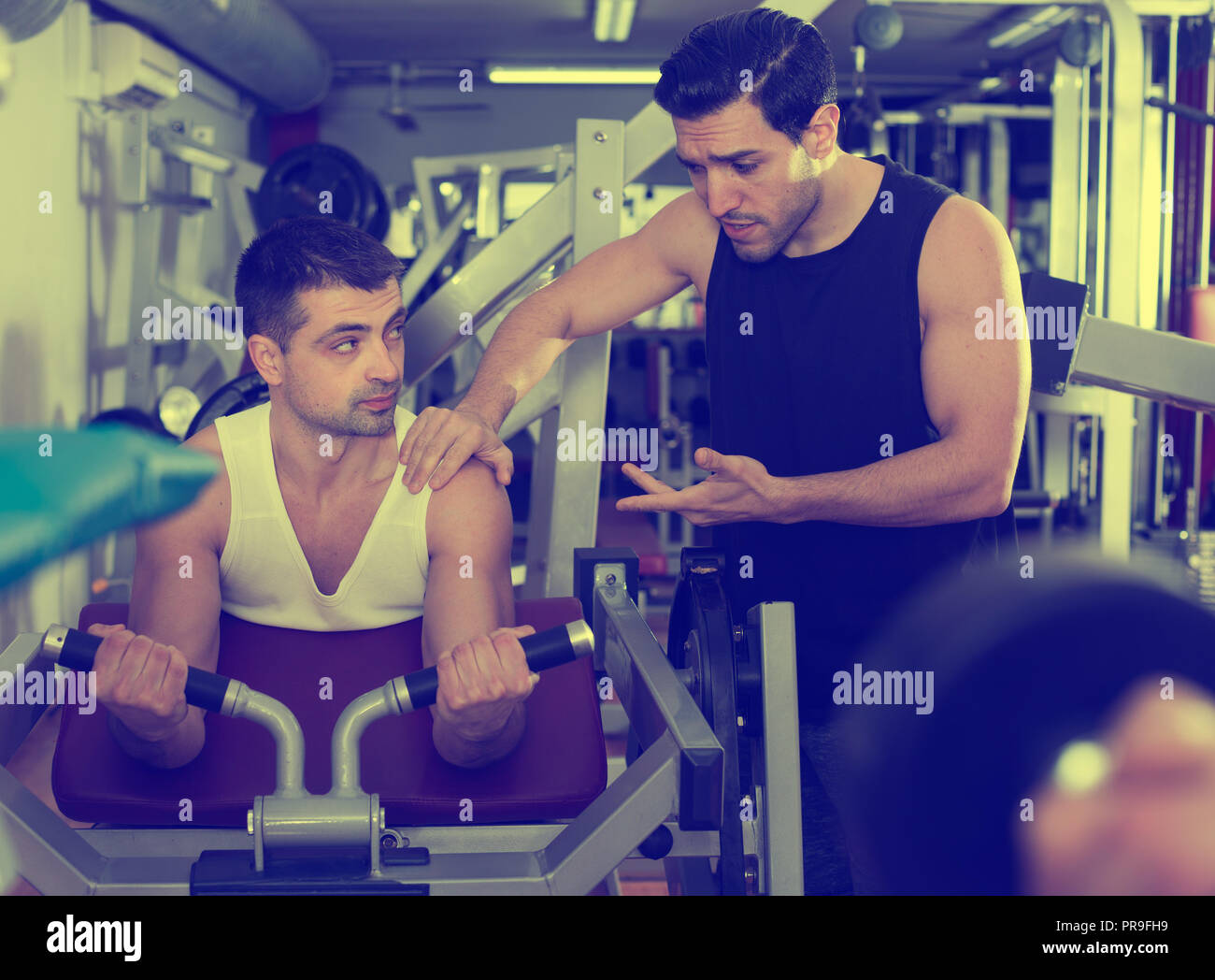 Male trainer explaining to muscular guy technique of performing ...