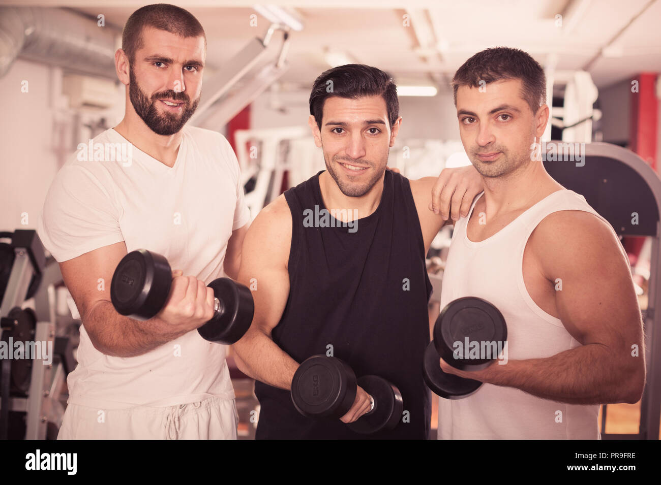Three muscular men taking break during workout in gym, posing together ...