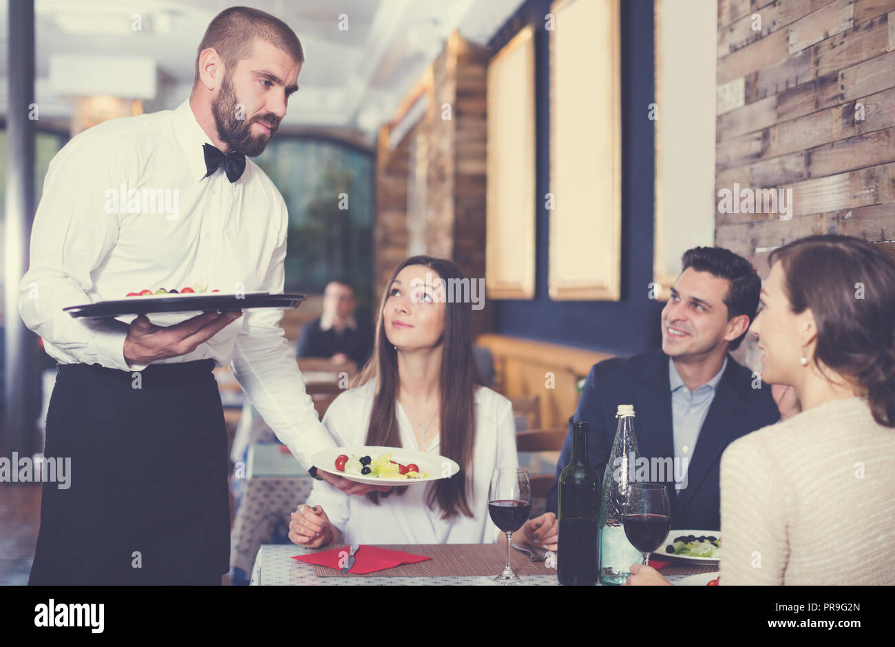 Waiter worker male bringing food for people of adult smiling visitors ...