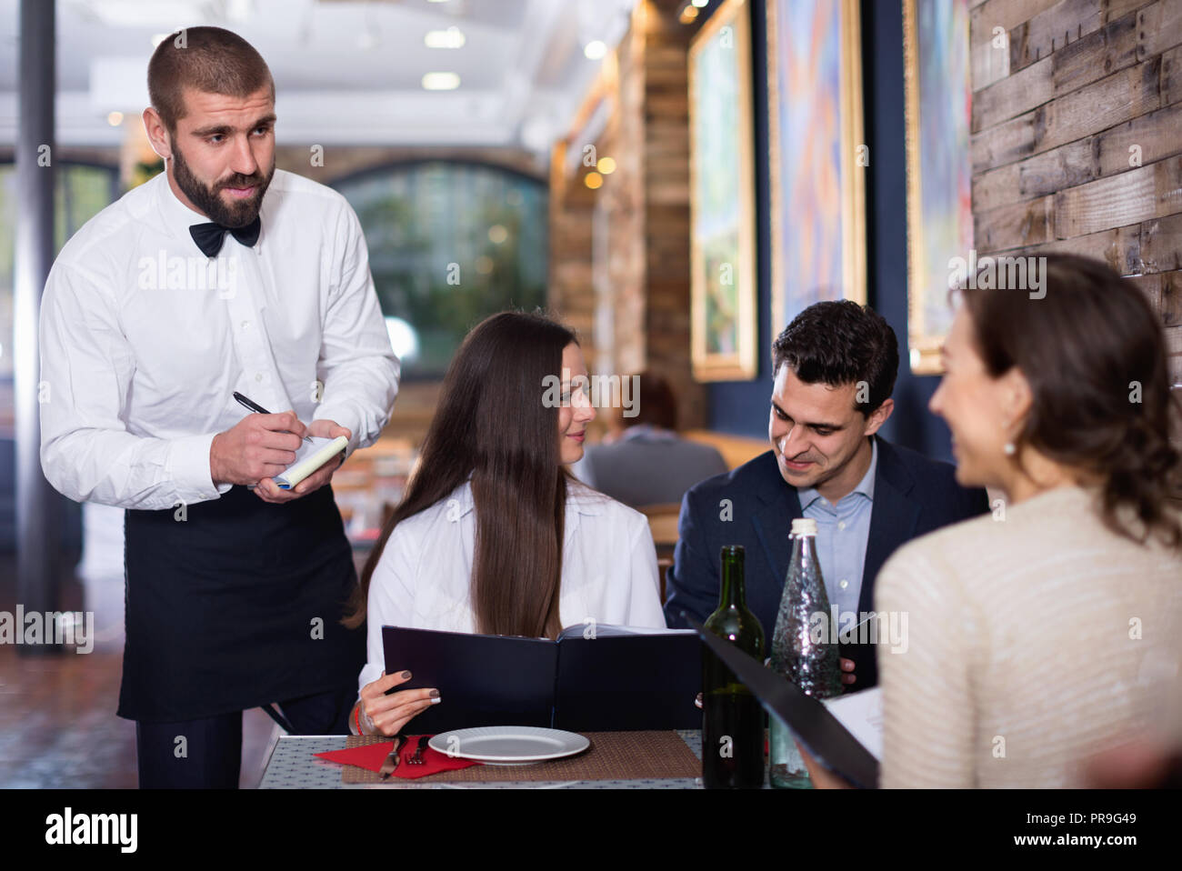 Diligent smiling pleasant waiter with notebook taking order from ...