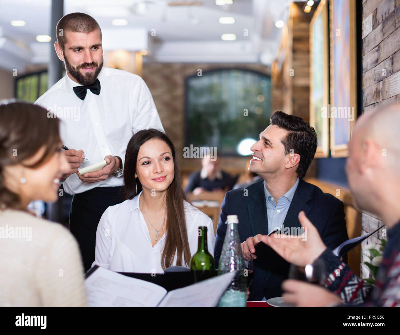 Diligent smiling waiter with notebook taking order from friendly ...