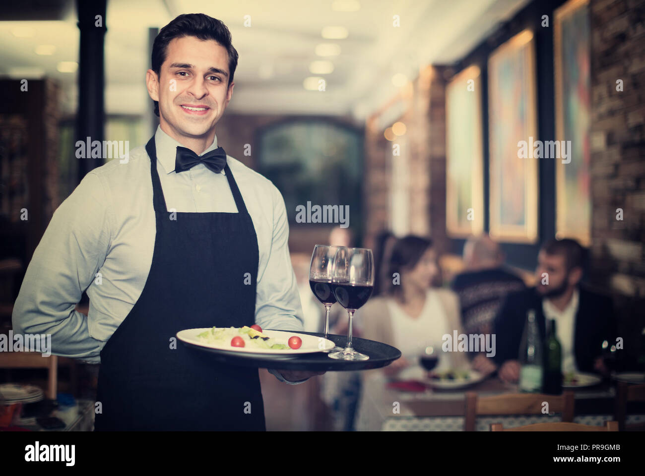 Professional friendly waiter holding serving tray for restaurant guests ...