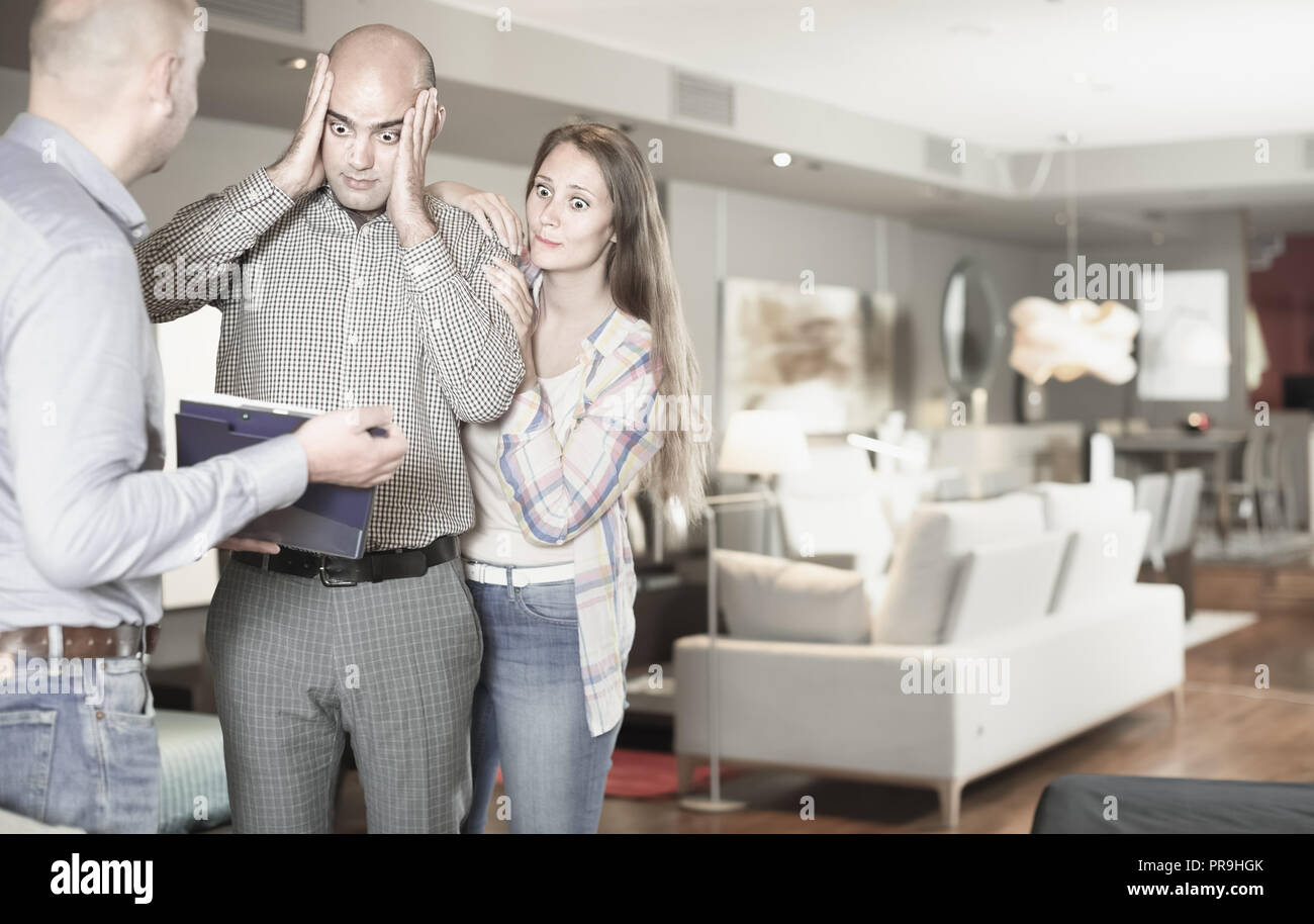 Young surprised and shocked couple watching price-list in furnishings ...