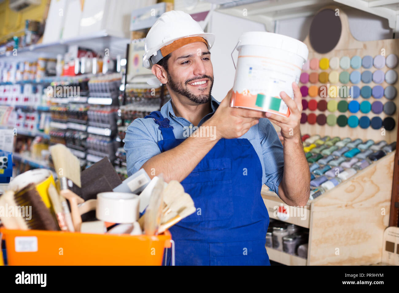 Smiling workman choosing materials for renovation works in paint store ...