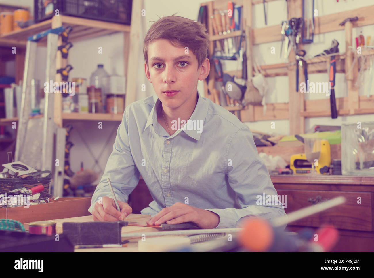 Handsome germany teenager smiling and working with wood in the workshop ...